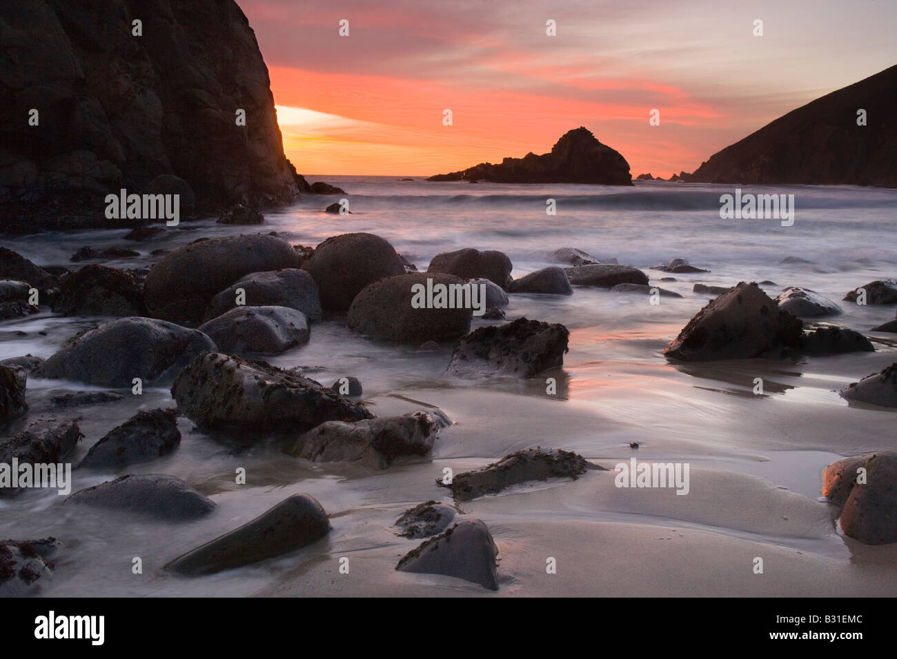 Dark rocks and sand reflect the warm light of sunset at Pfeiffer Beach ...