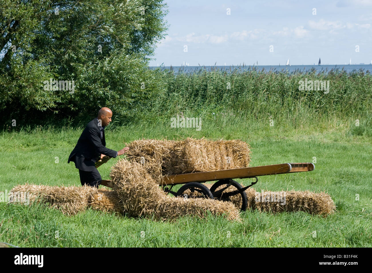 Dark man in suit standing at old hay wagon with round hay bales Stock ...