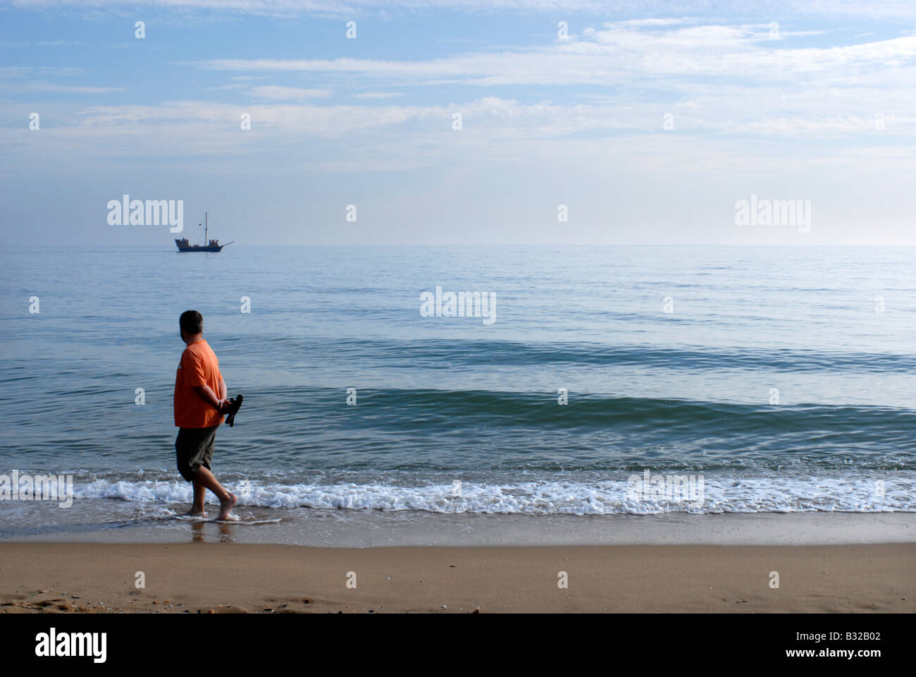 Strolling man looking out at sea towards a fishing boat at Golden Sands ...