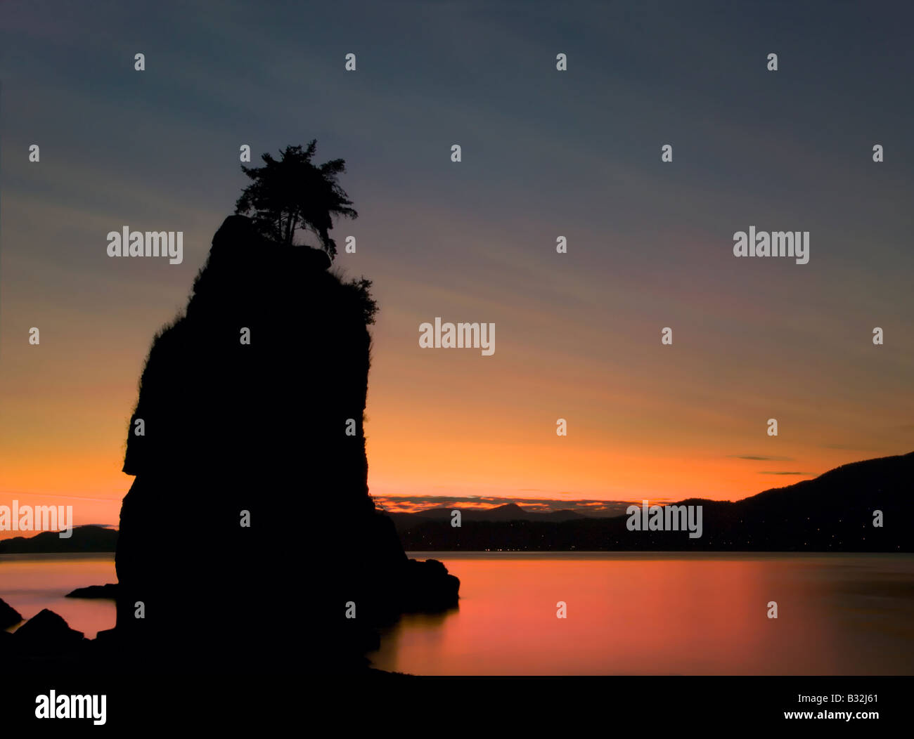 The setting Sun makes a orange glow behind the famous Siwash rock in ...