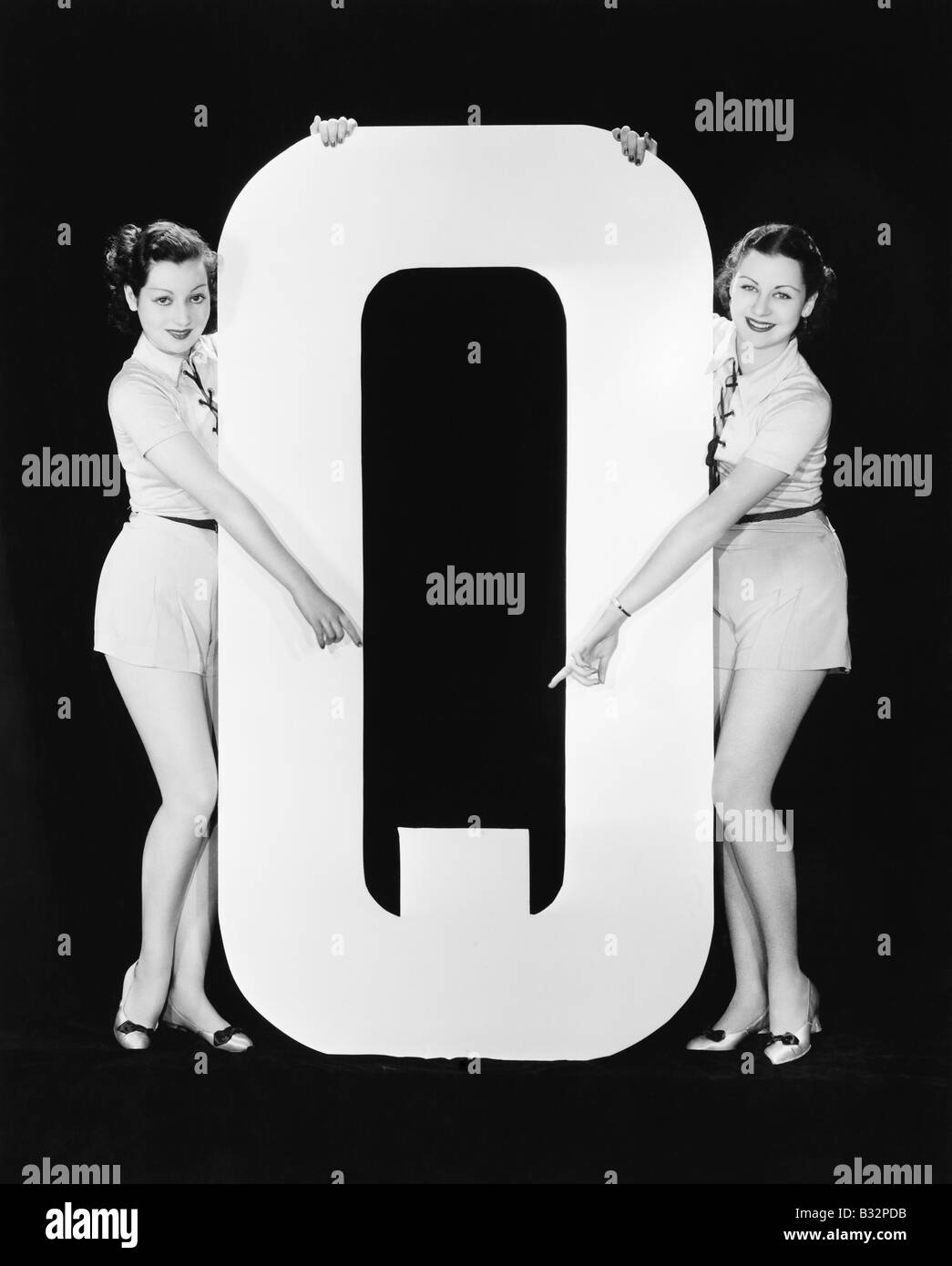 Two women pointing at huge letter Q Stock Photo - Alamy