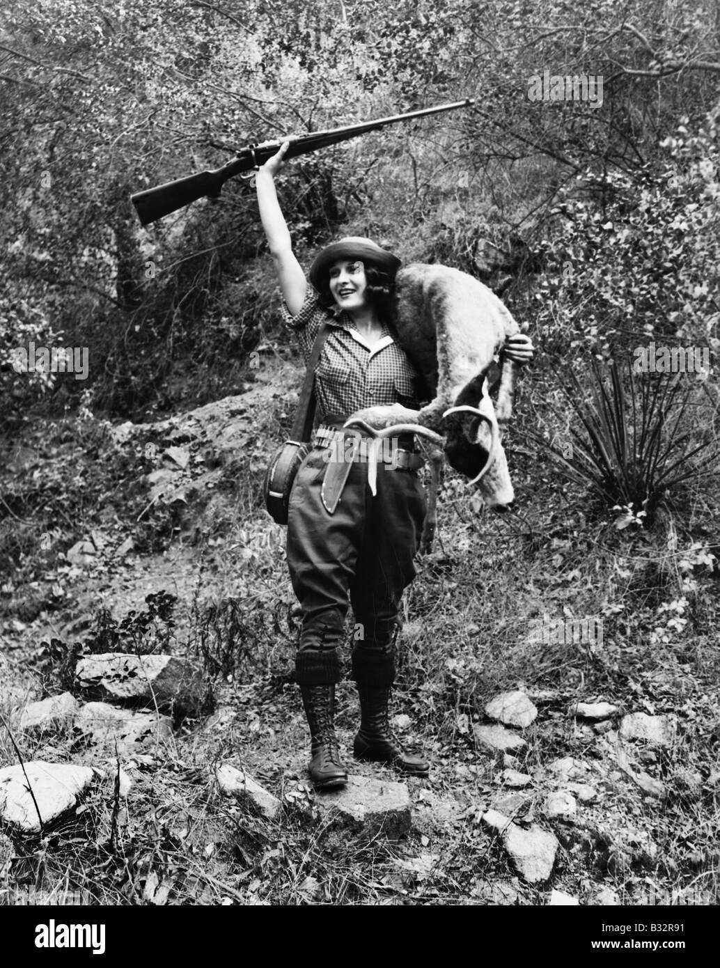 Oh deer, a young female hunter with gun raised high smiles with a young ...