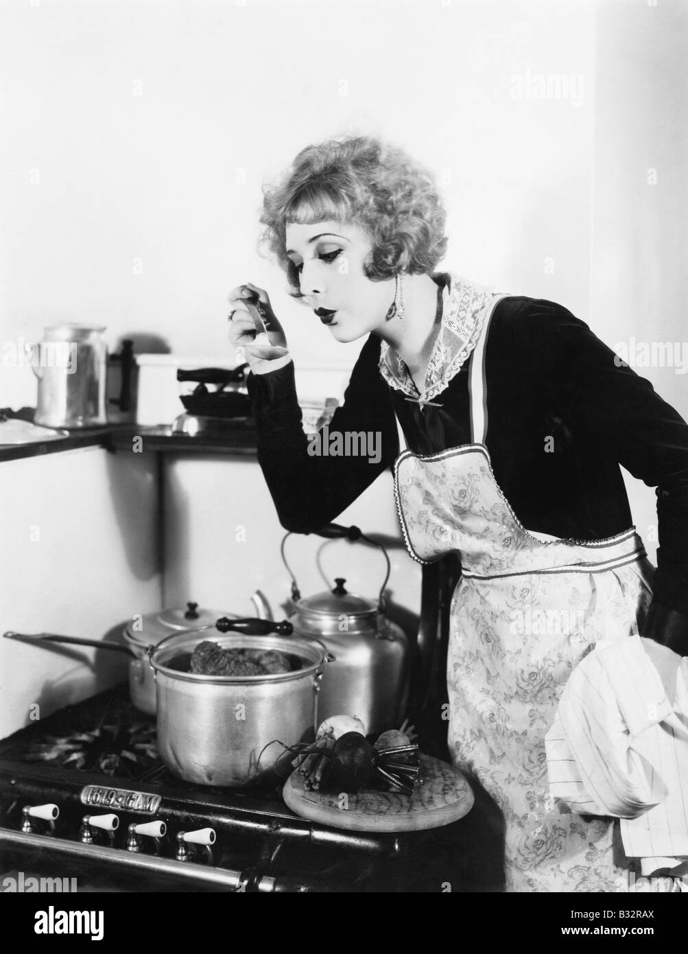 Young Woman In An Apron In Her Kitchen Tasting Her Food From A Pot