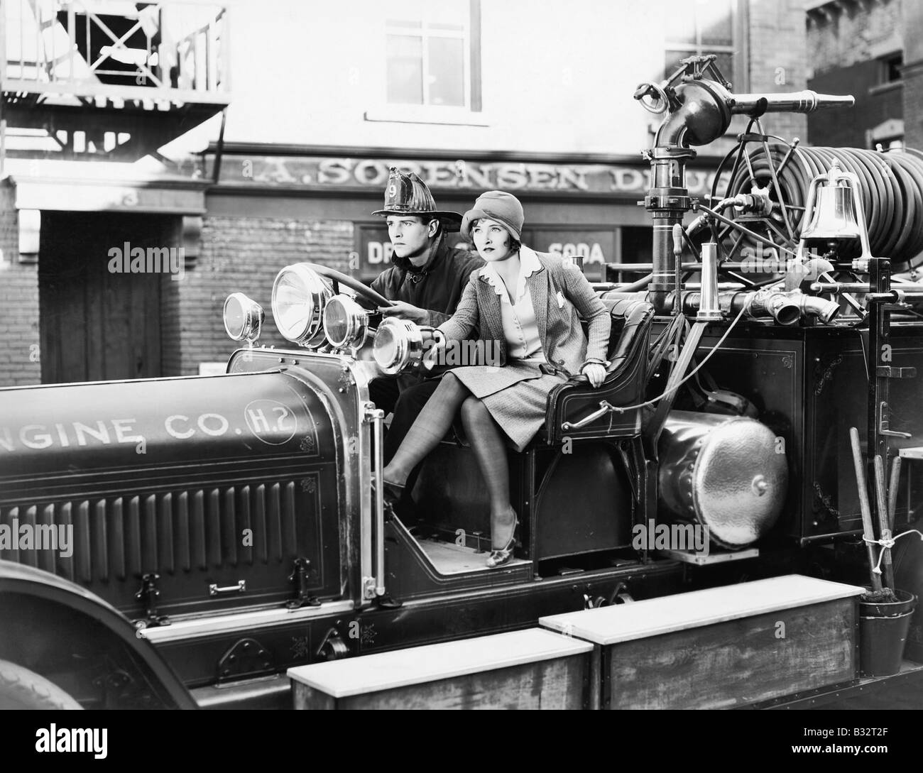 Firefighter driving a fire engine and a young woman sitting beside him ...