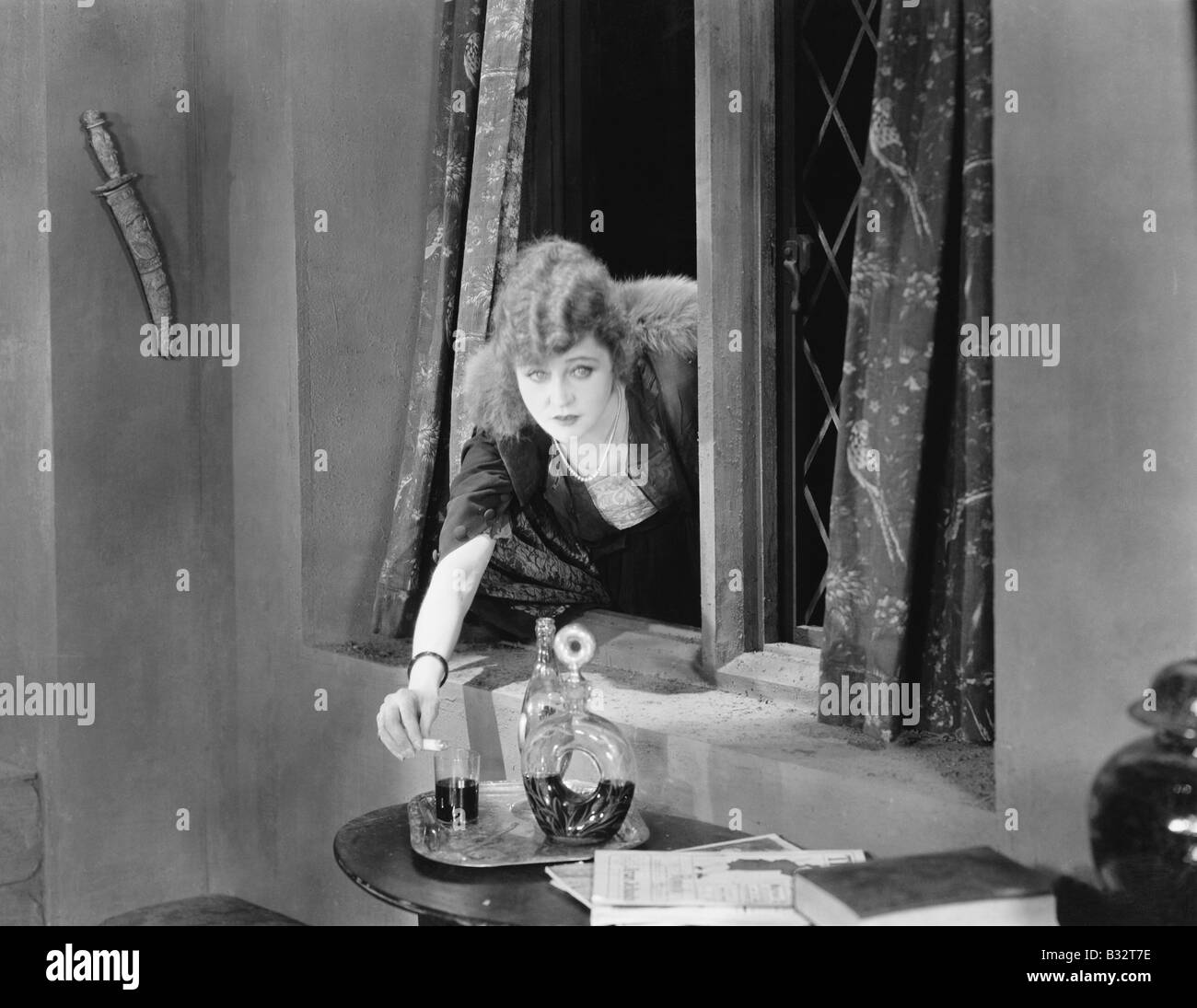 Portrait of a young woman reaching through a window and pouring poison ...