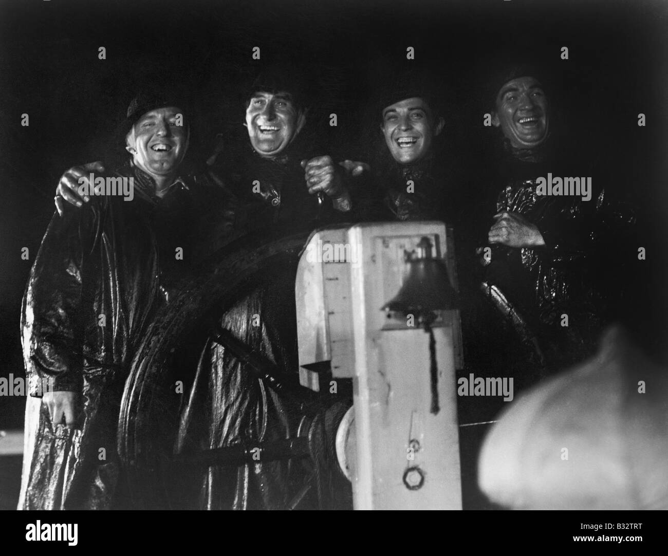 Four men in slickers standing together at the captain's wheel of a ship ...