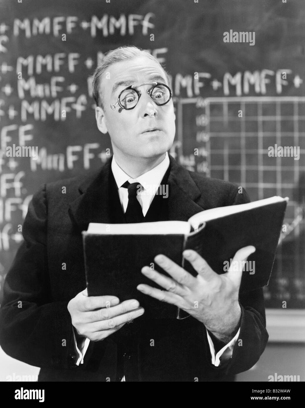 Teacher holding a book in front of a black board looking surprised ...