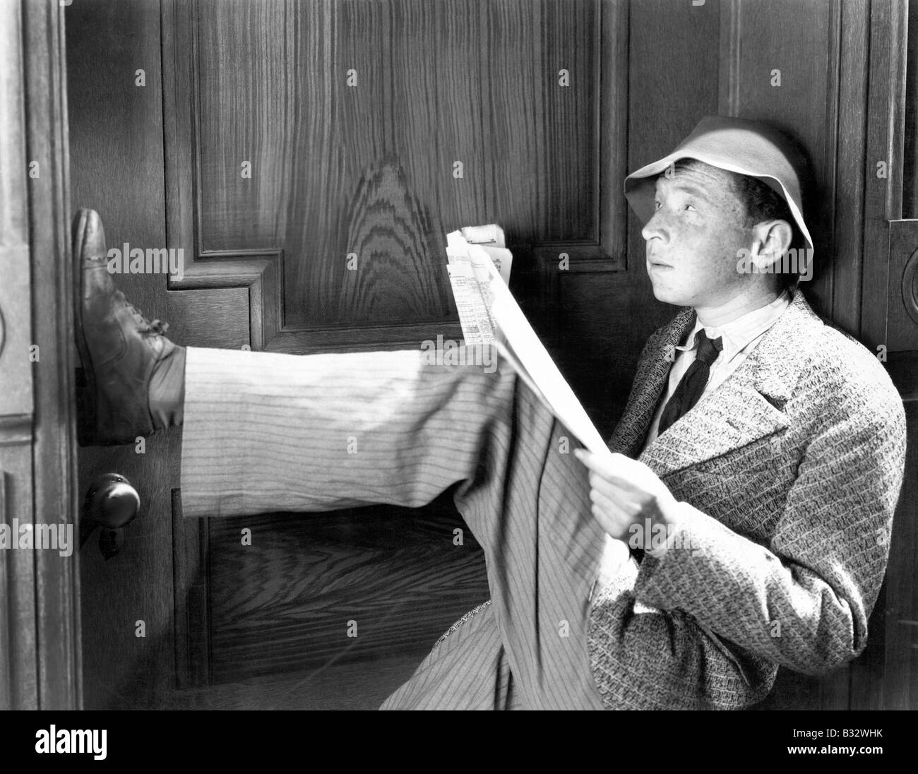 Man leaning against a door with his legs up and reading a newspaper ...