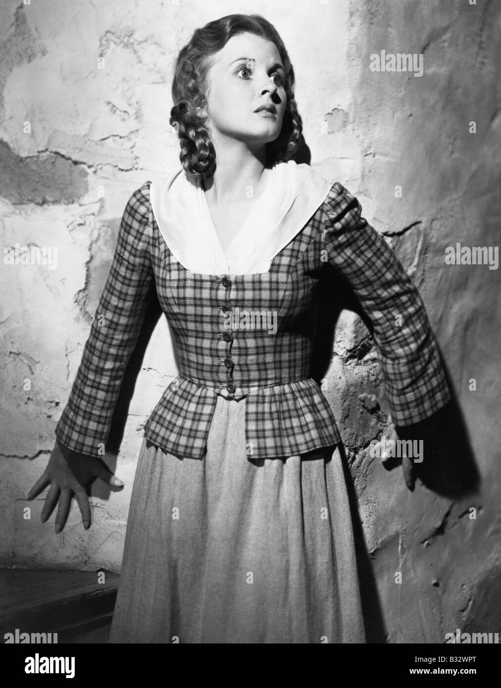 Young woman leaning against a wall and looking scared Stock Photo - Alamy