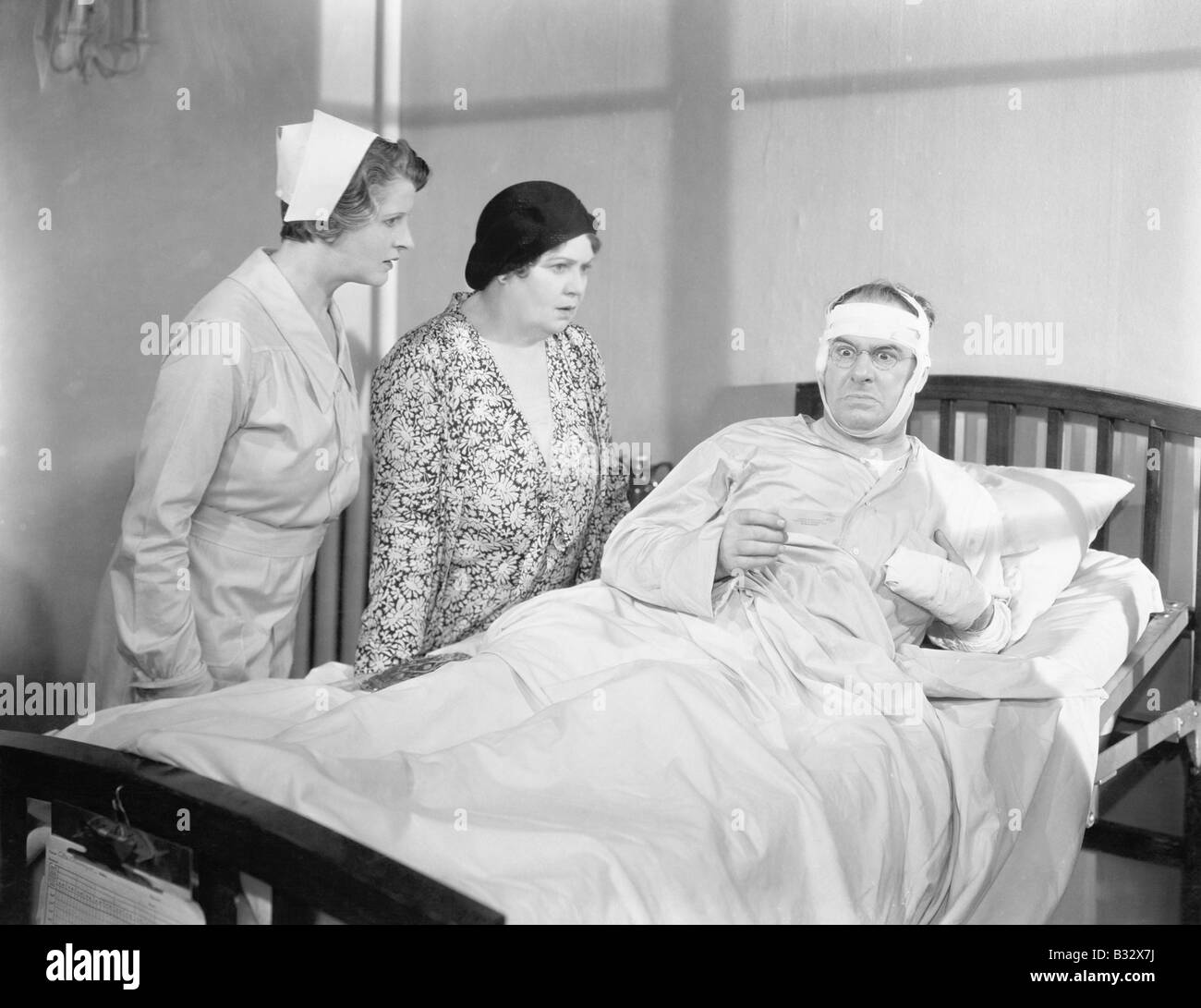A Wife Next To Her Husband In A Hospital Bed With A Nurse Attending a-wife-next-to-her-husband-in-a-hospital-bed-with-a-nurse-attending