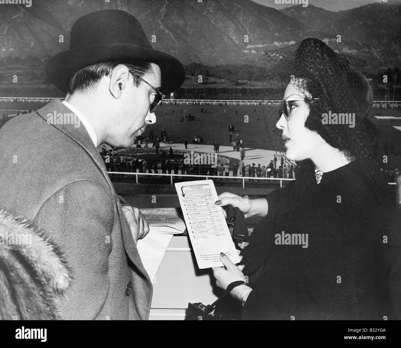 Elegant couple at horse race looking at program Stock Photo - Alamy