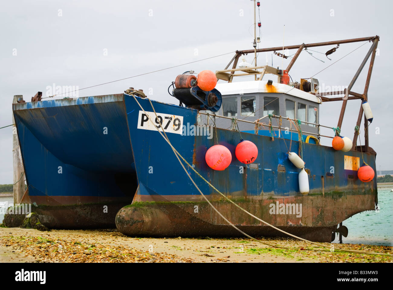 Port side view of an old blue trawler with bright orange buoys. Low ...