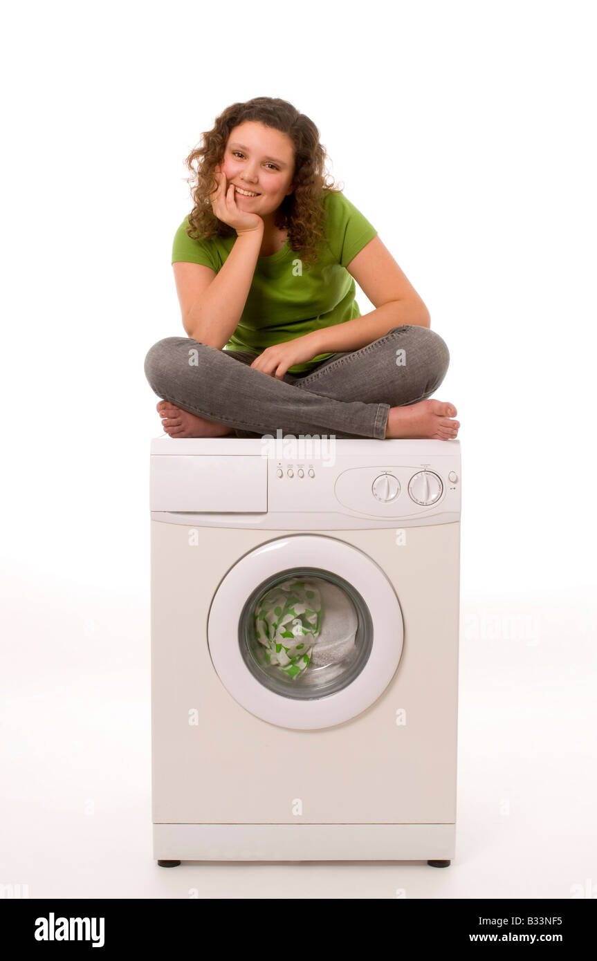 Young girl in green top sat on top of washing machine looking happy ...