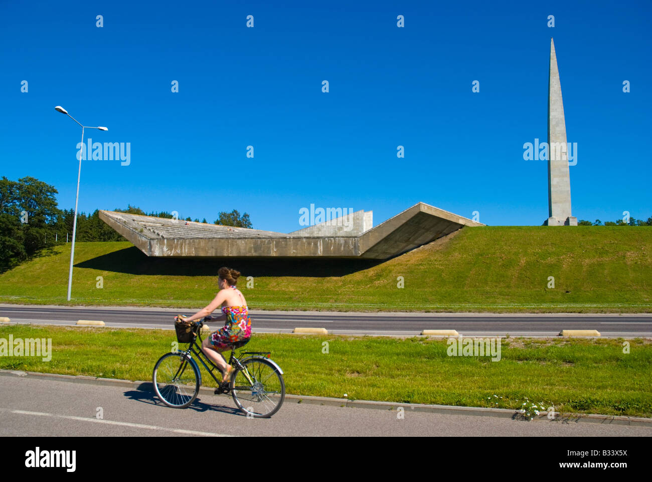 Woman cycling past Soviet war memorial along Pirita tee road in Tallinn ...