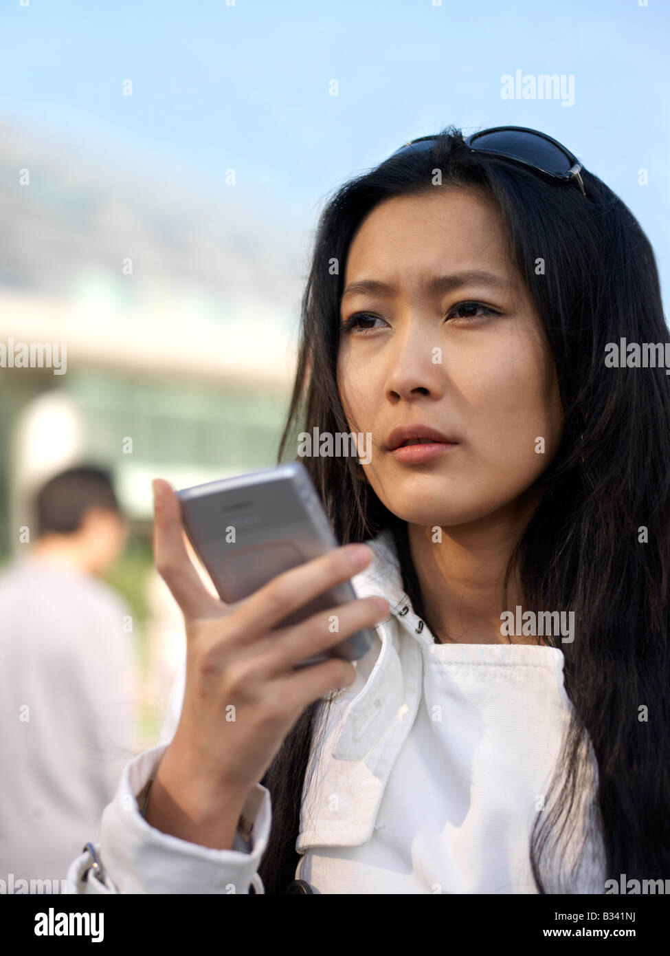 A young Chinese business woman using her mobile phone PDA in the city ...