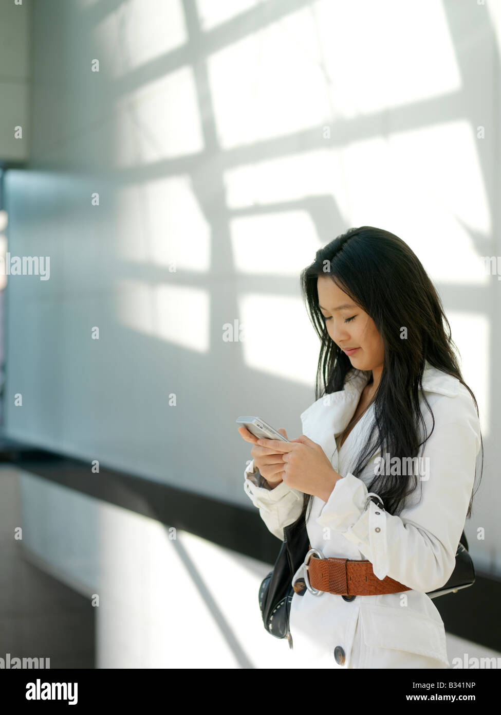 A young Chinese business woman using her mobile phone PDA in the city ...
