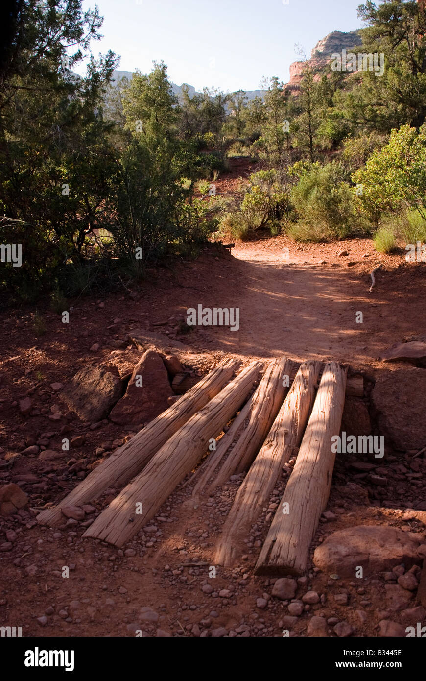 Rough tree log bridge covered in red sand, spans a dry creek bed on the ...