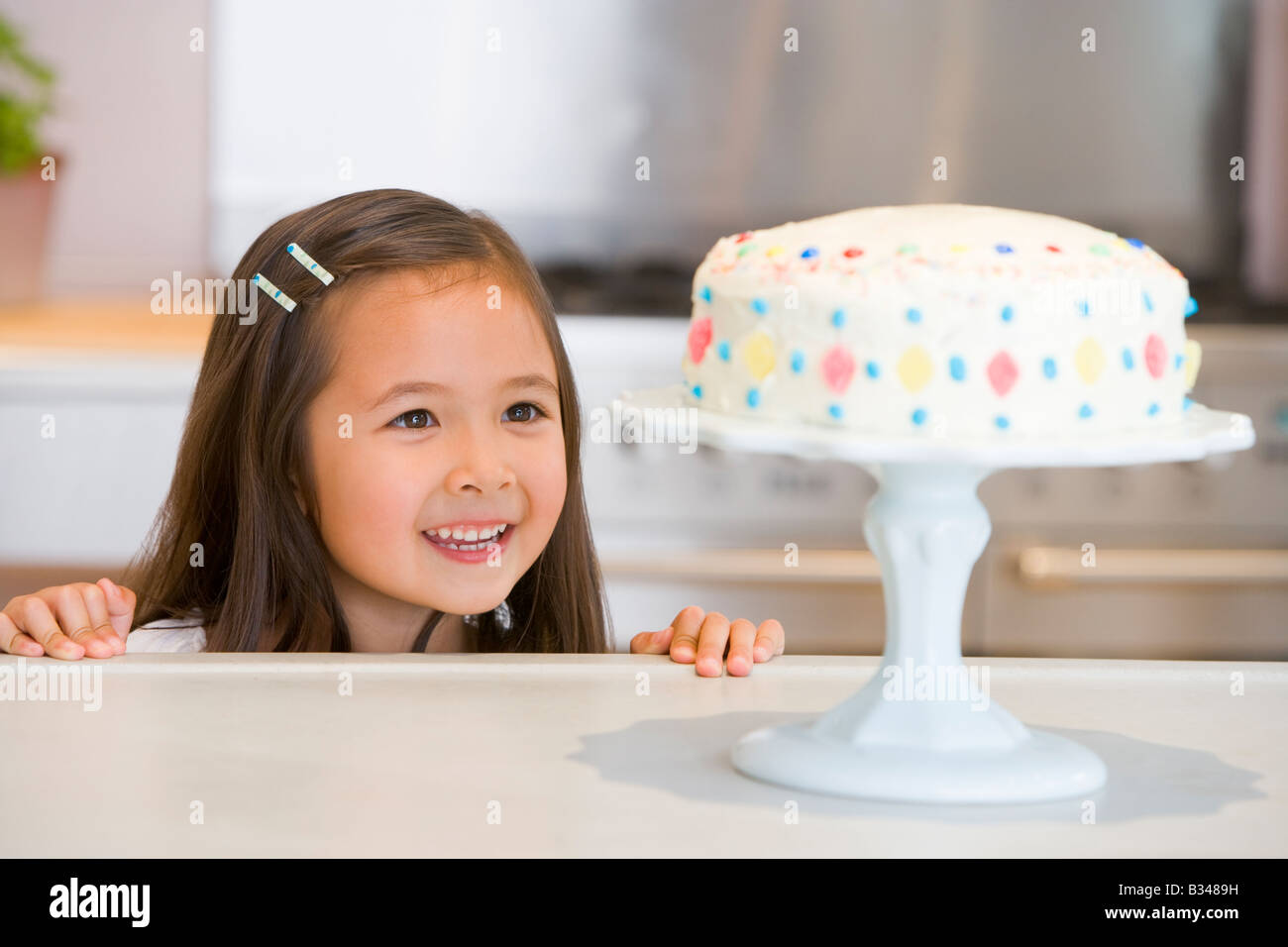 Young girl at kitchen counter looking at cake smiling Stock Photo - Alamy