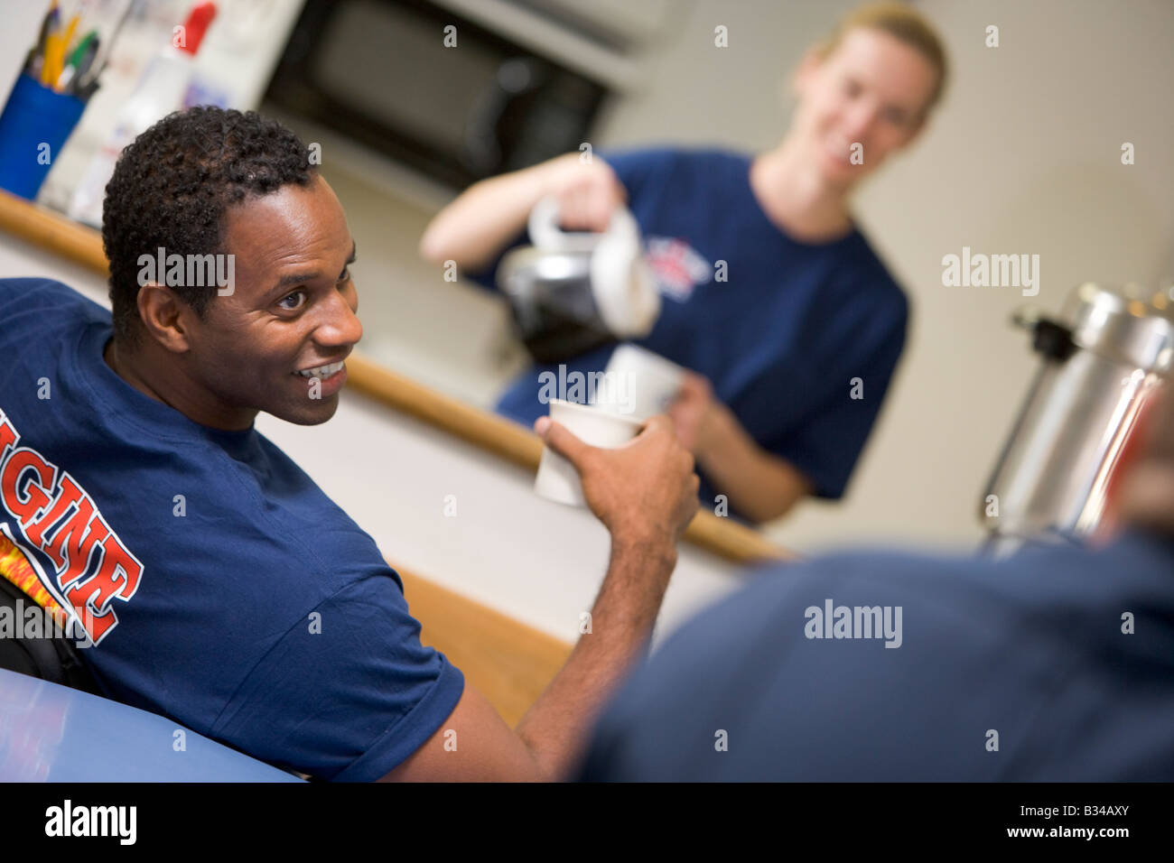 Three firefighters in break room with one getting coffee in background ...
