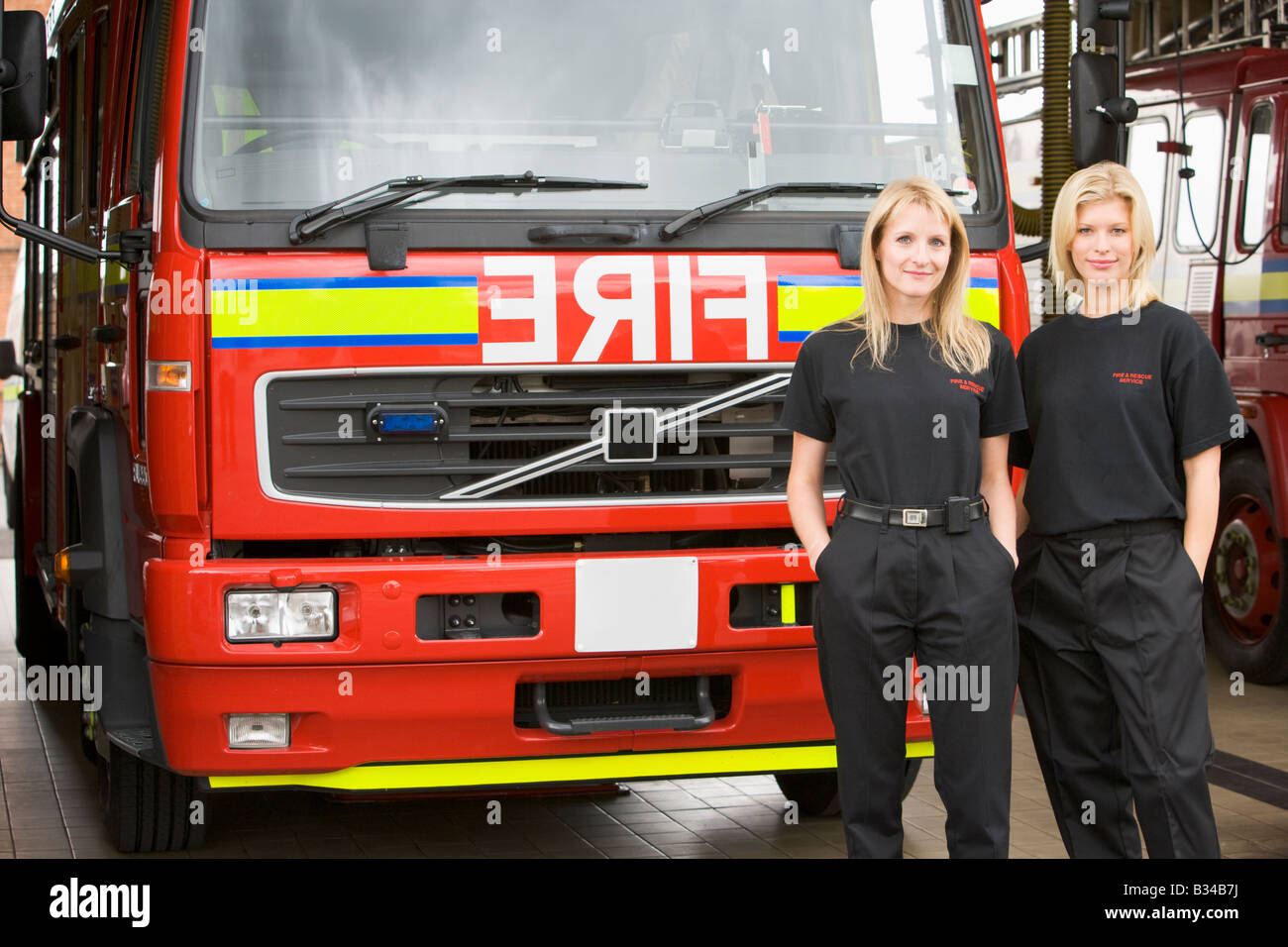 Two firefighters standing in front of fire engine Stock Photo - Alamy