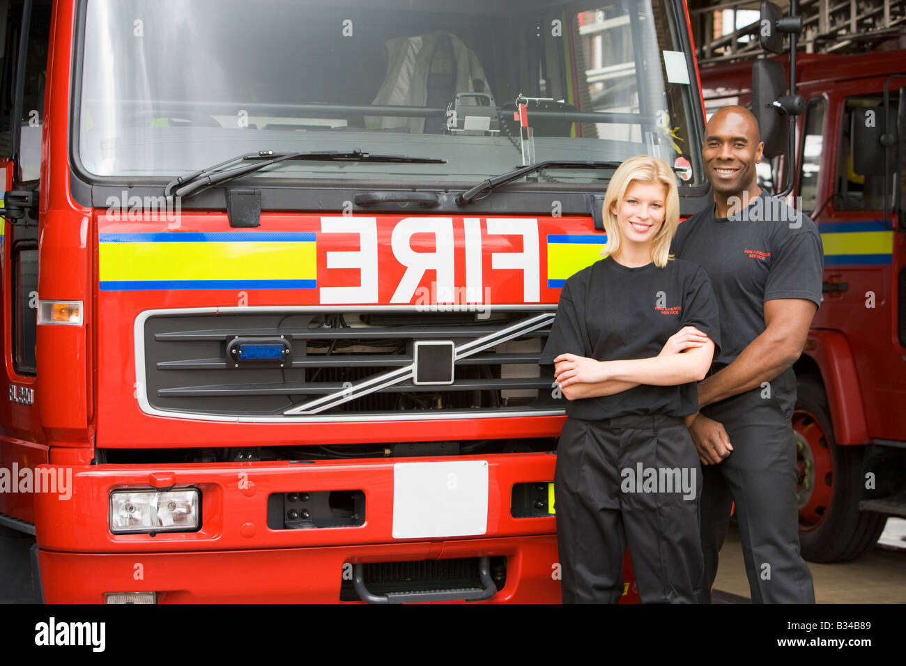 Two firefighters standing in front of fire engine Stock Photo - Alamy