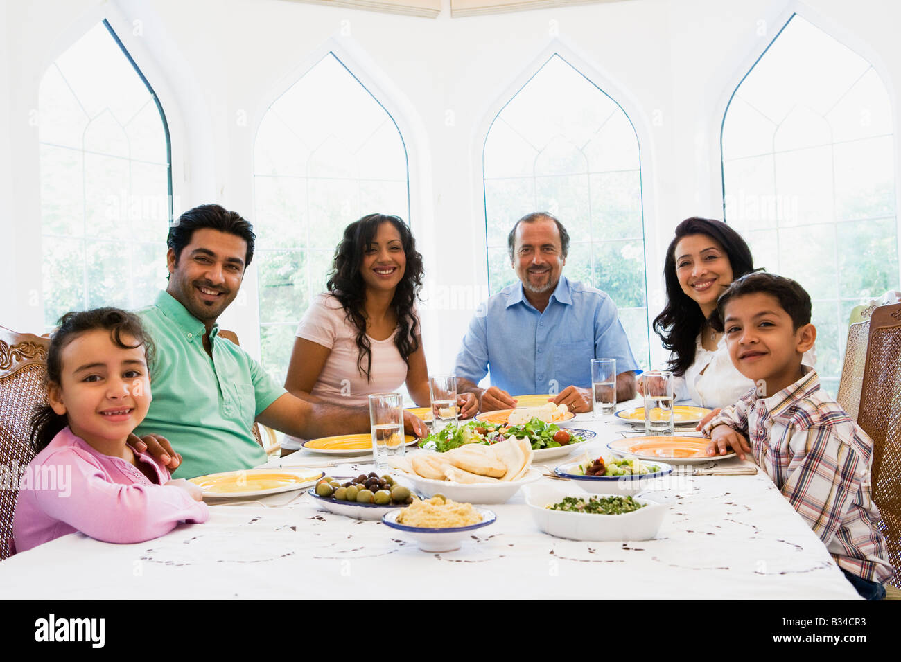 Family sitting at dinner table smiling (high key Stock Photo - Alamy