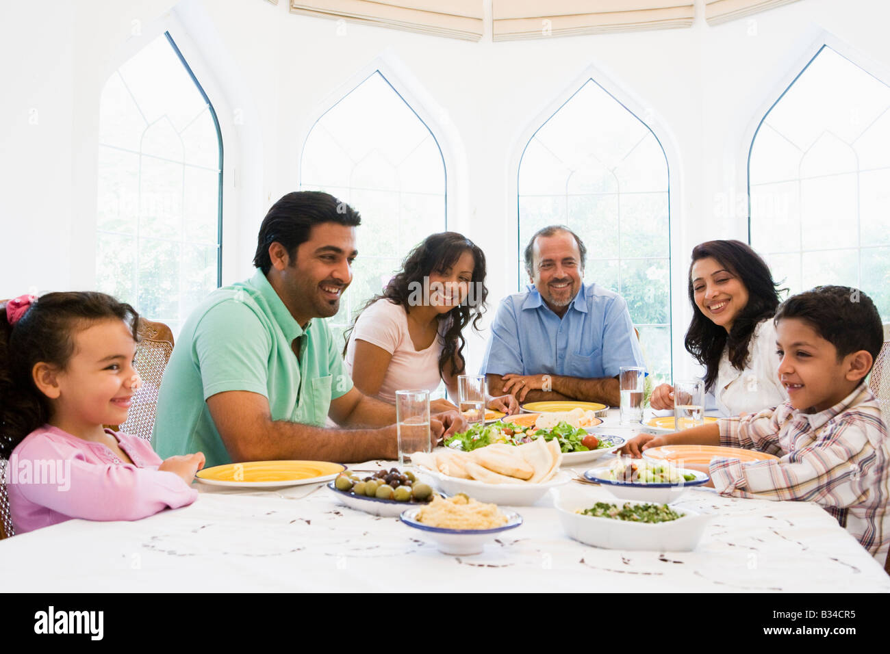 Family sitting at dinner table smiling (high key Stock Photo - Alamy