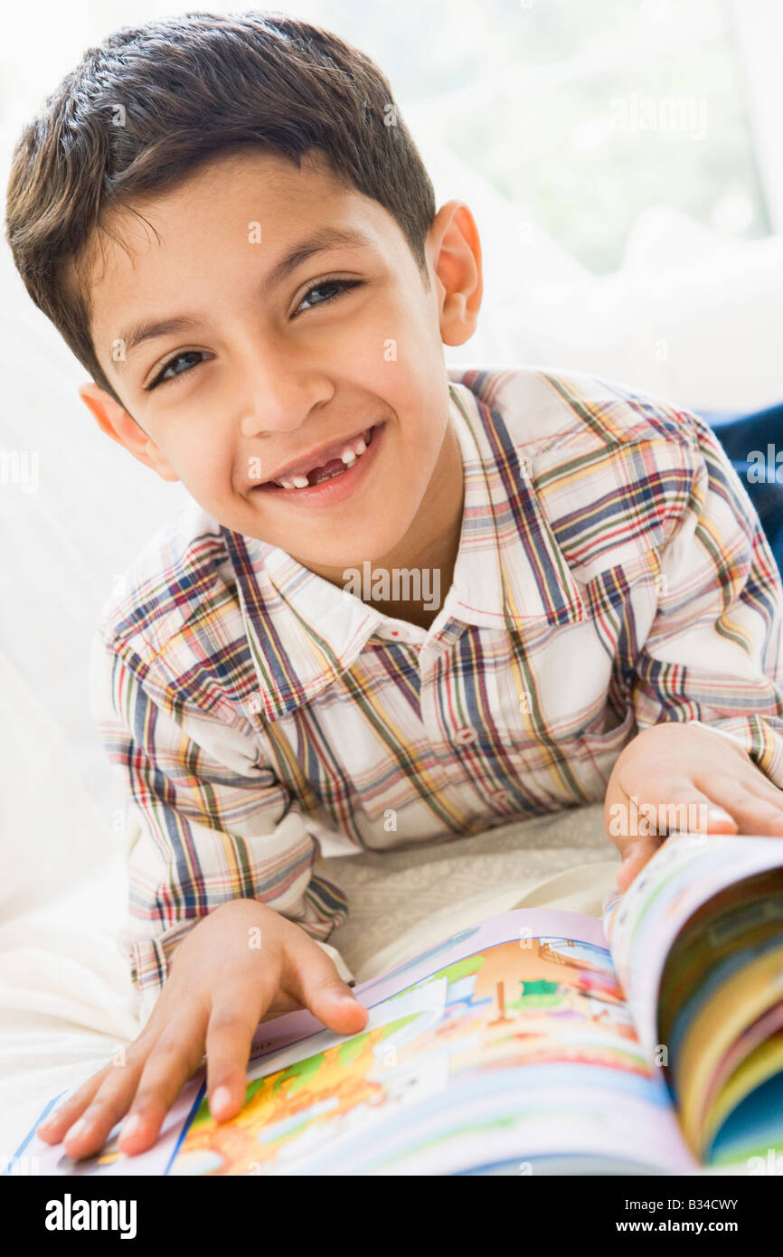 Young boy in living room reading a book and smiling (high key Stock ...