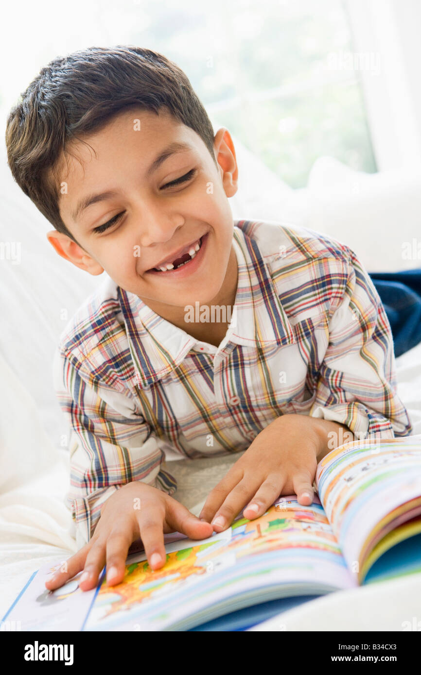 Young boy in living room reading a book and smiling (high key Stock ...