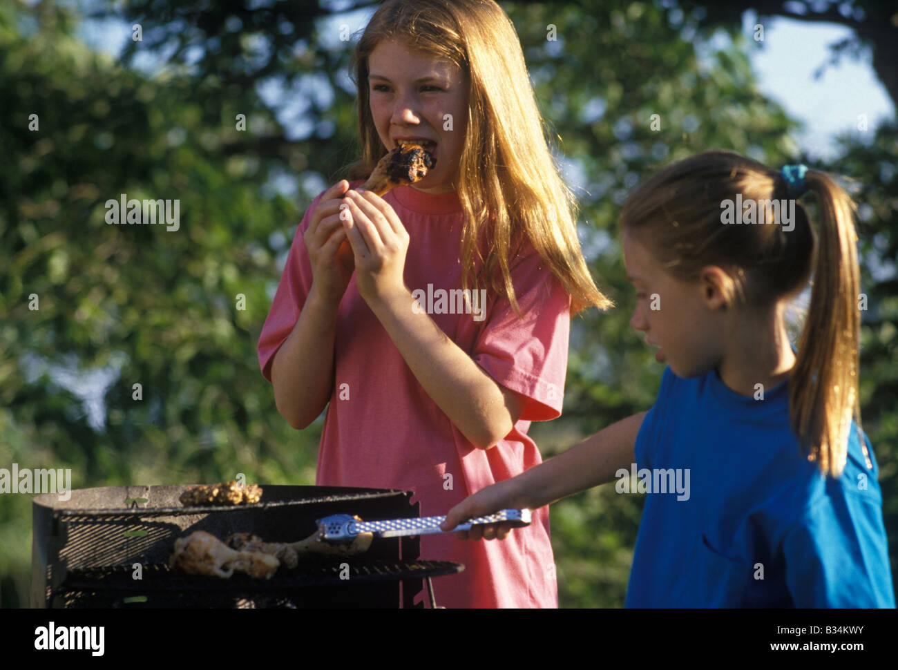 two girls barbecuing chicken in the garden with the chicken looking ...