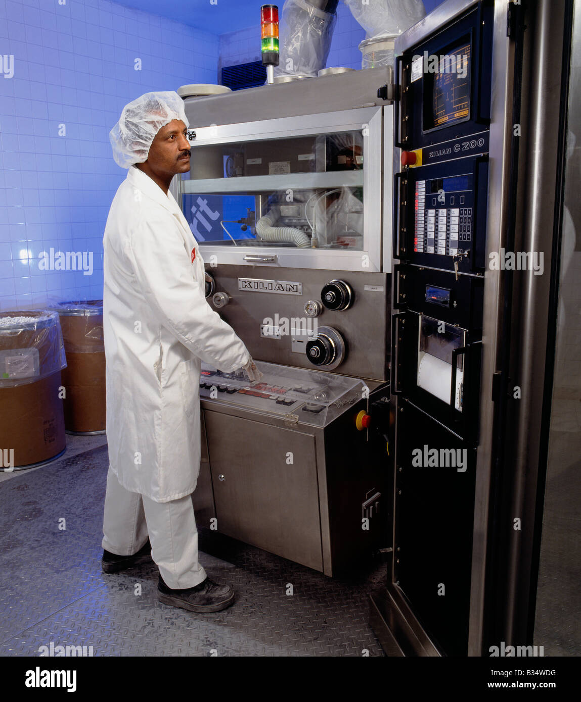 Worker operating machinery used to produce tablets in a pharmaceutical ...