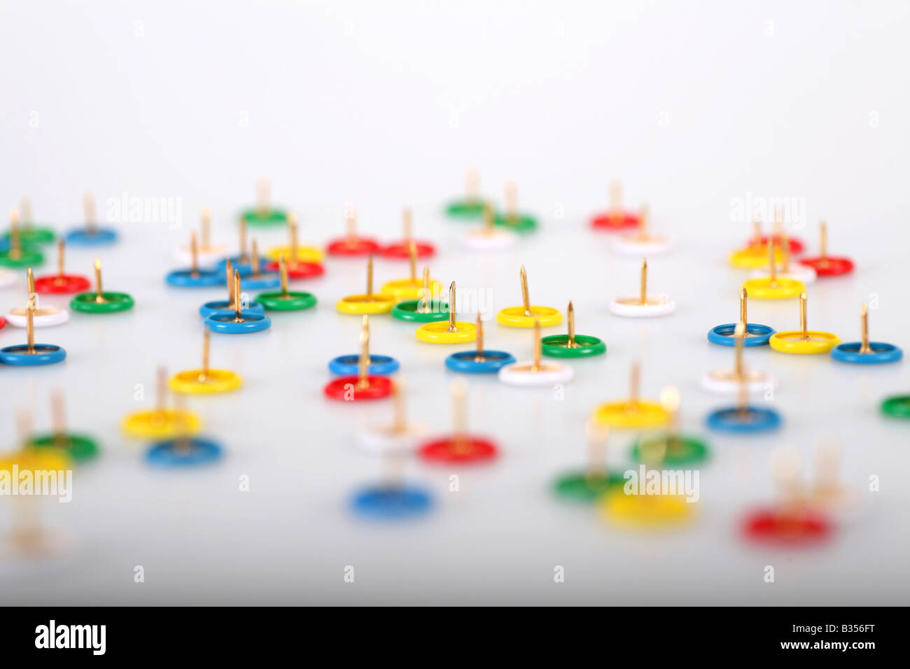 Upturned brass drawing pins with colored thumbnail on a white ...