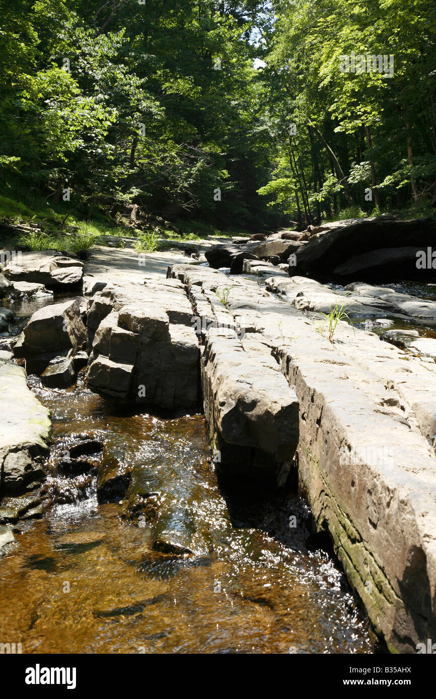 Flat layers of rock lay in a broken sheet with small stream flowing ...
