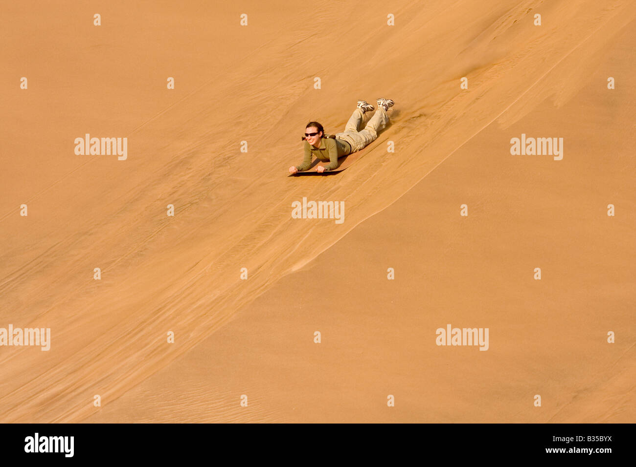 A tourist woman sandboards by sliding down a sand dune on a polished ...