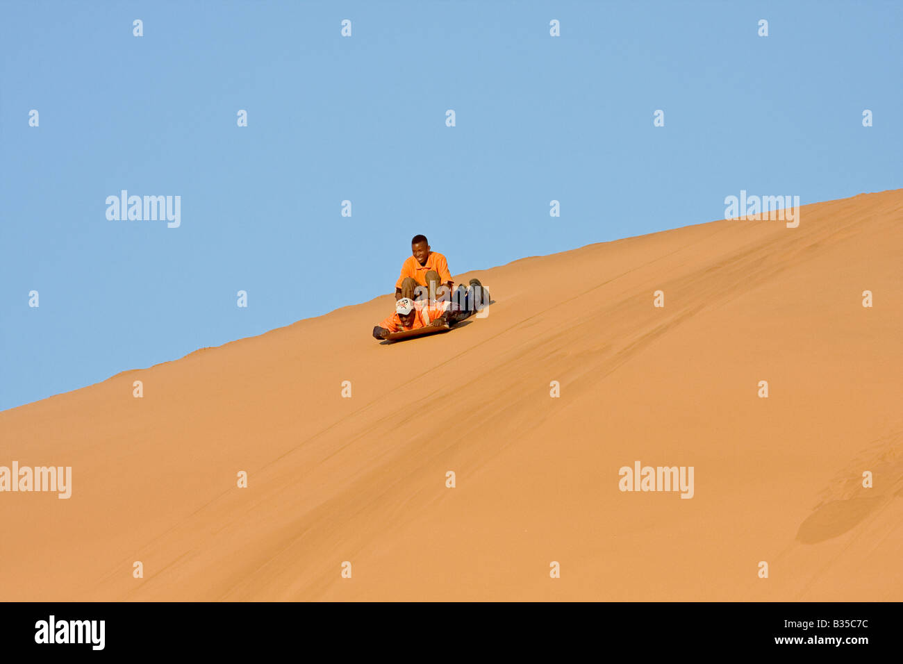 Two local men sandboard by sliding down a sand dune on a polished board ...