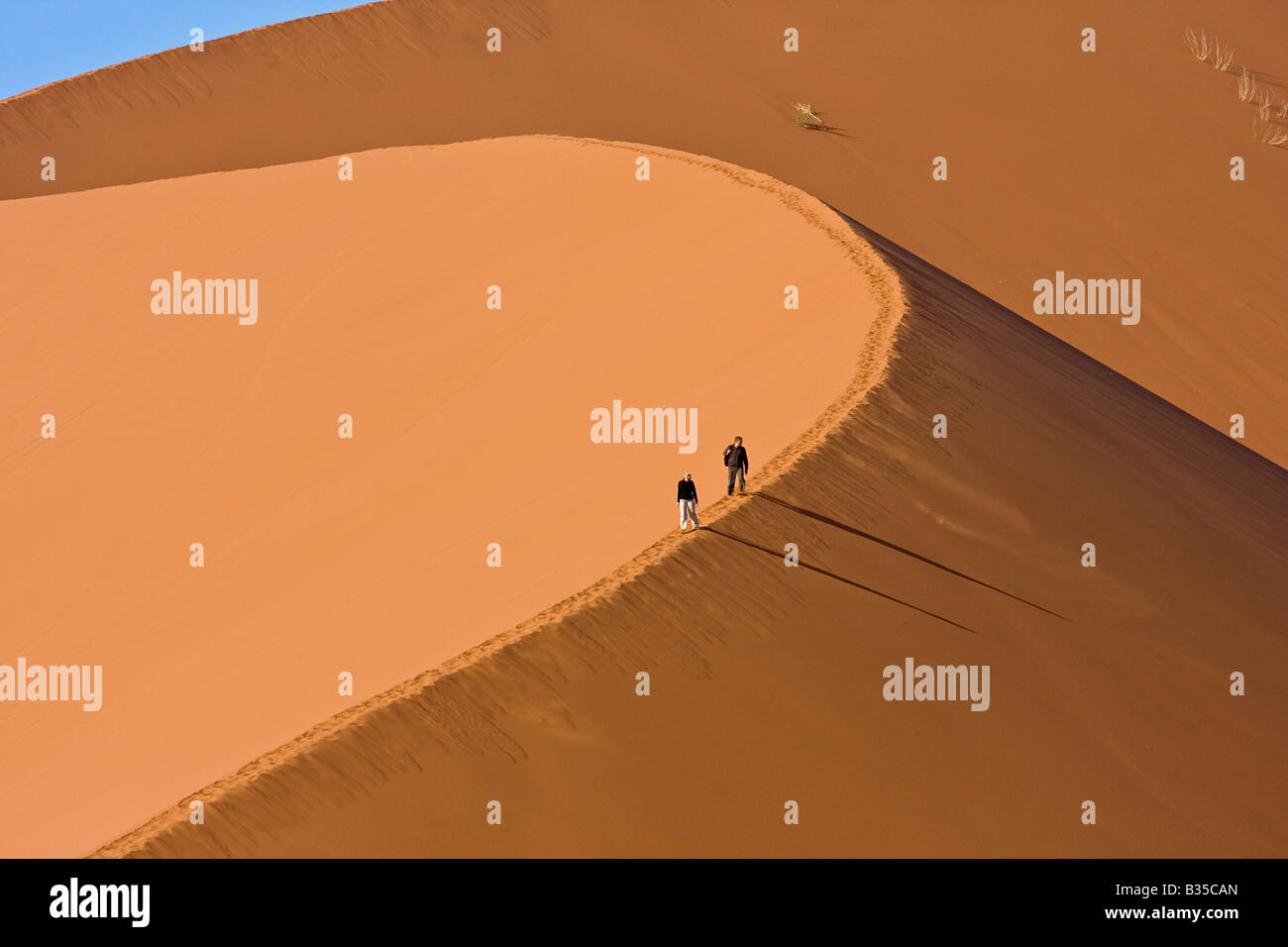 Man and woman walk atop sand dunes of Sossusvlei in the Namib Naukluft ...