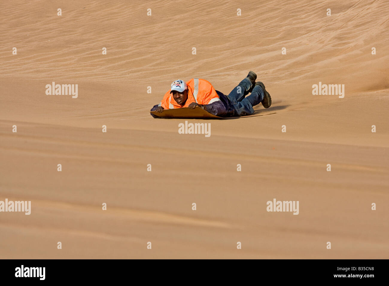 A local man sandboards by sliding down a sand dune on a polished board ...