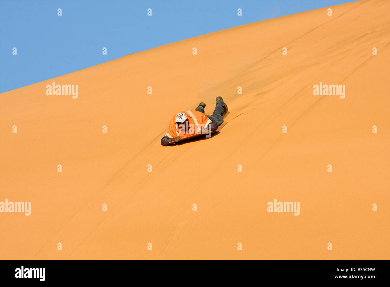 A local man sandboards by sliding down a sand dune on a polished board ...
