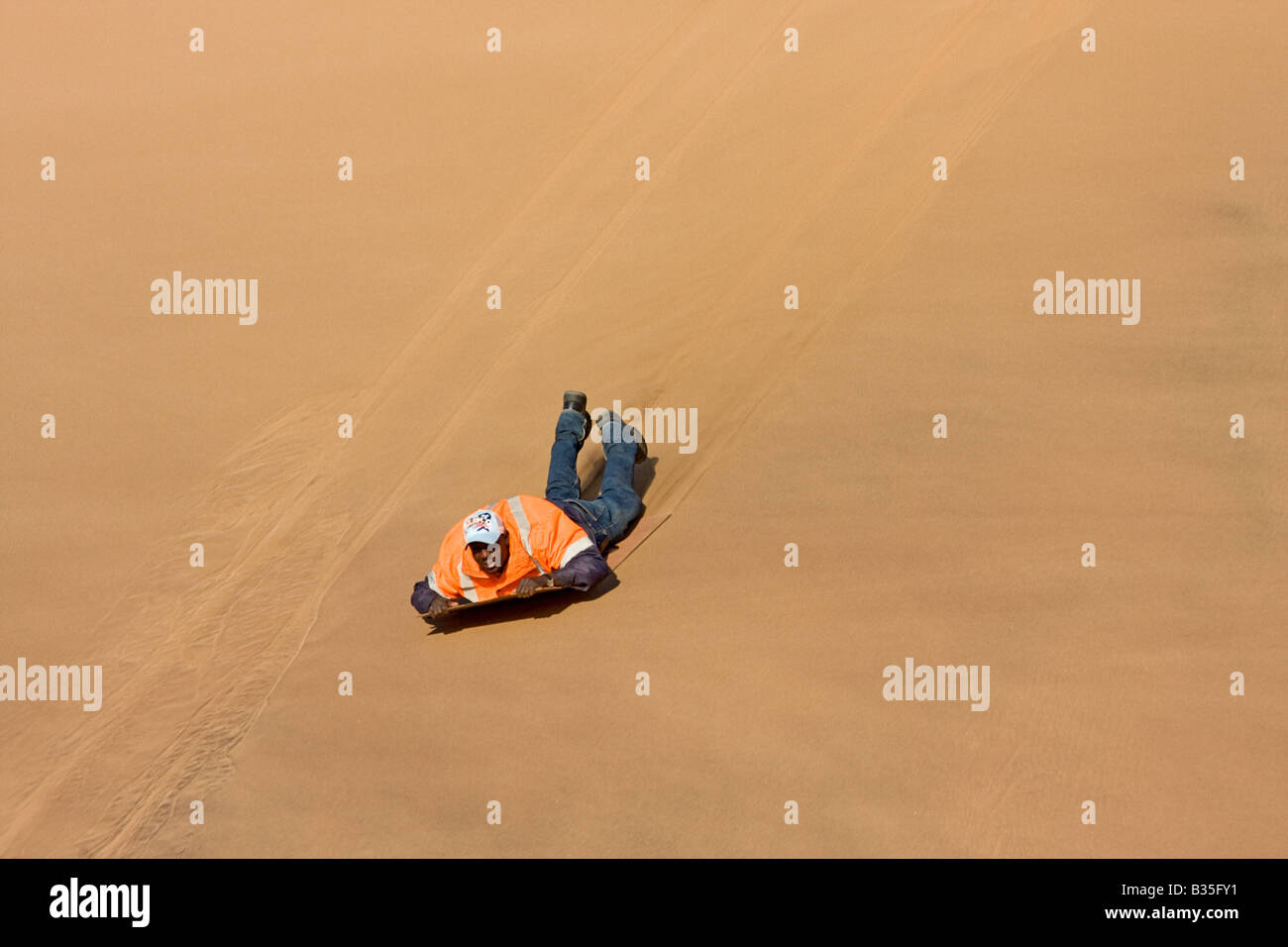 A local man sandboards by sliding down a sand dune on a polished board ...