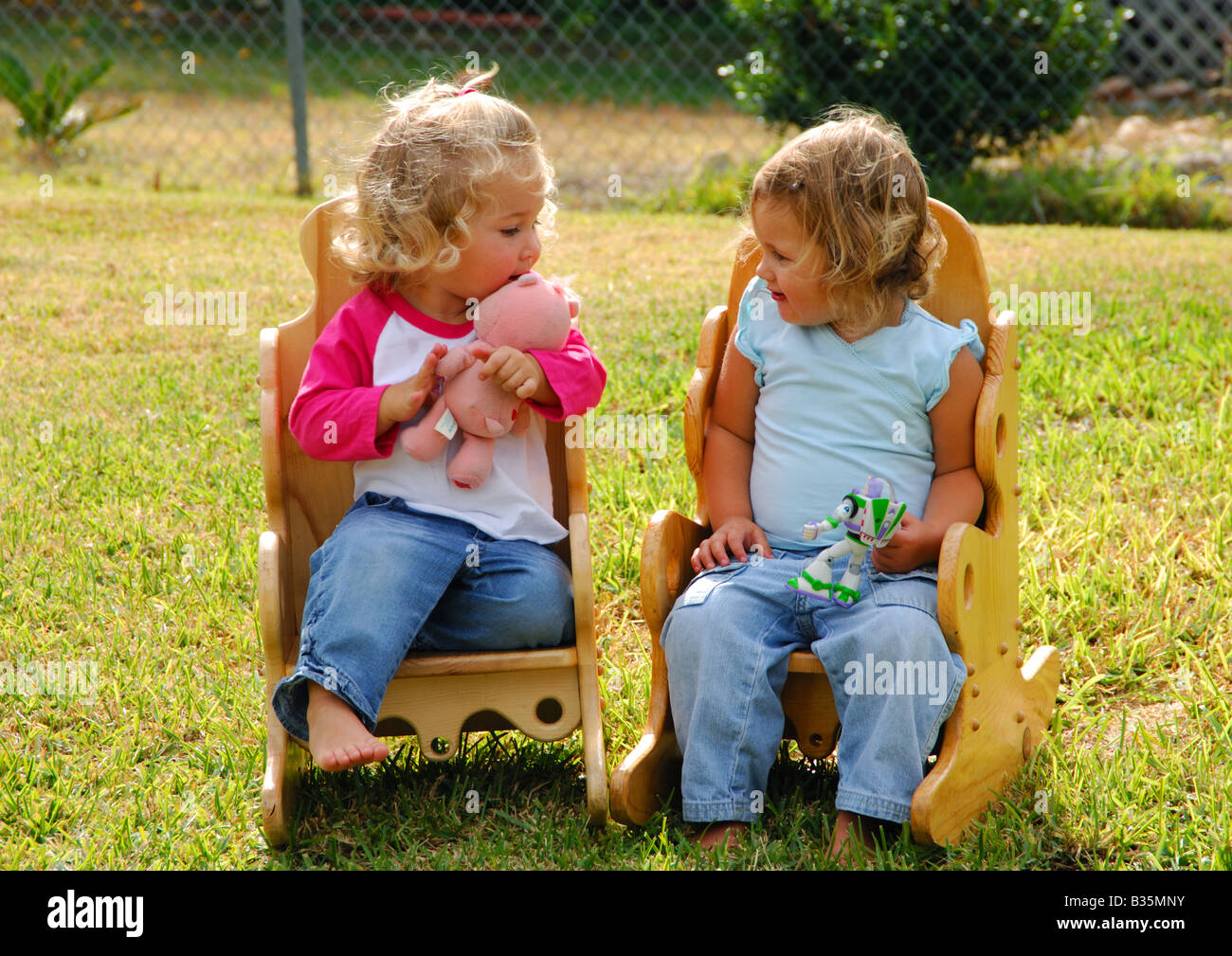 Two girls sitting on chairs and holding toys Stock Photo - Alamy