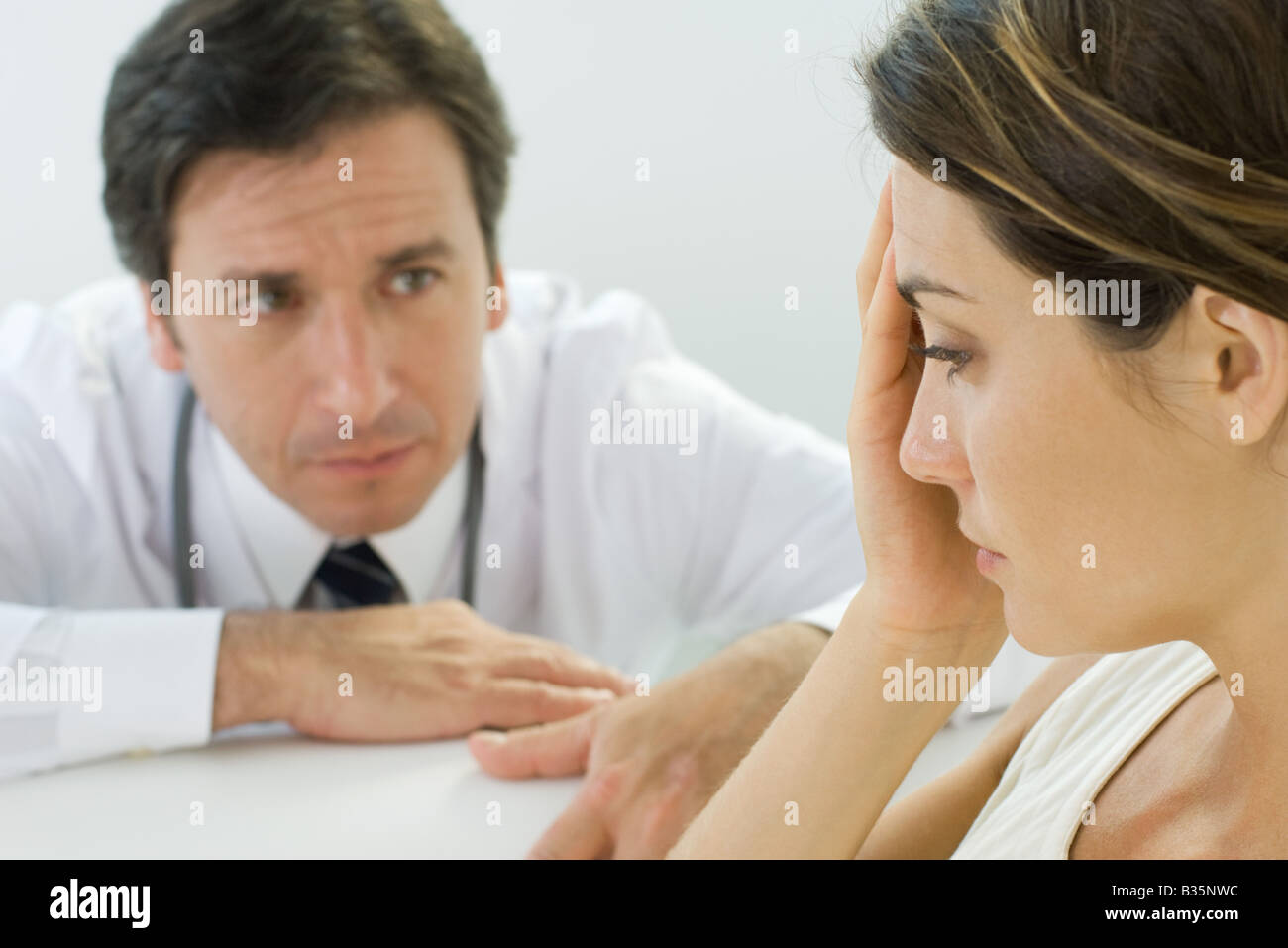 Woman holding head, looking down, concerned doctor in background Stock ...