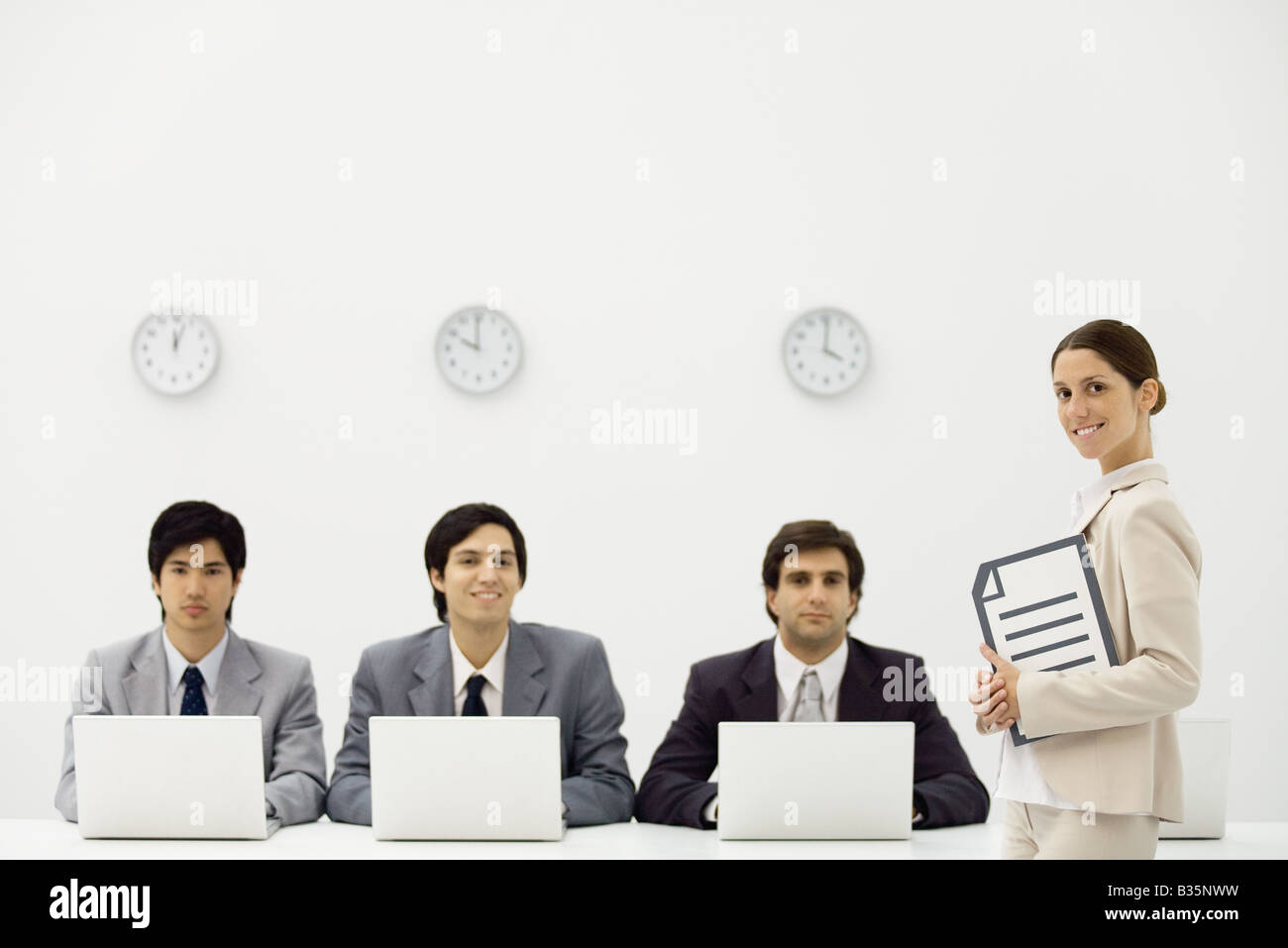 Professional men sitting with laptop computers beneath wall clocks ...