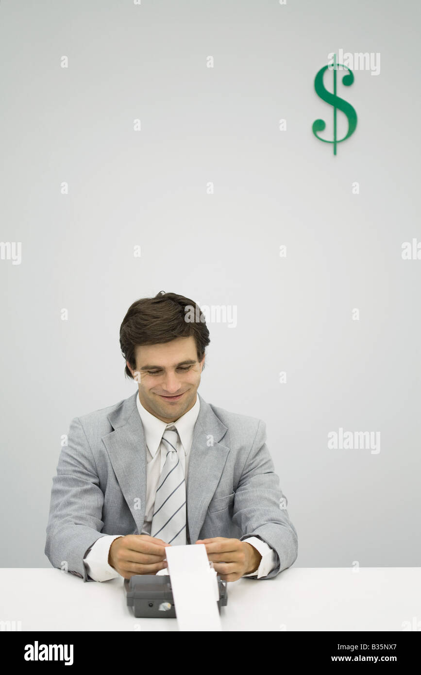 Accountant using adding machine, smiling, dollar sign on wall behind ...