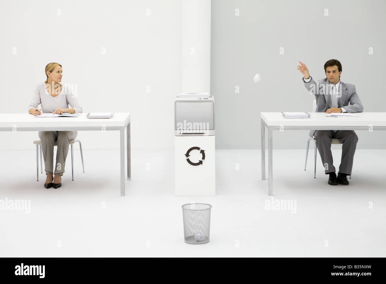 Male office worker throwing paper ball into trash can, female colleague ...