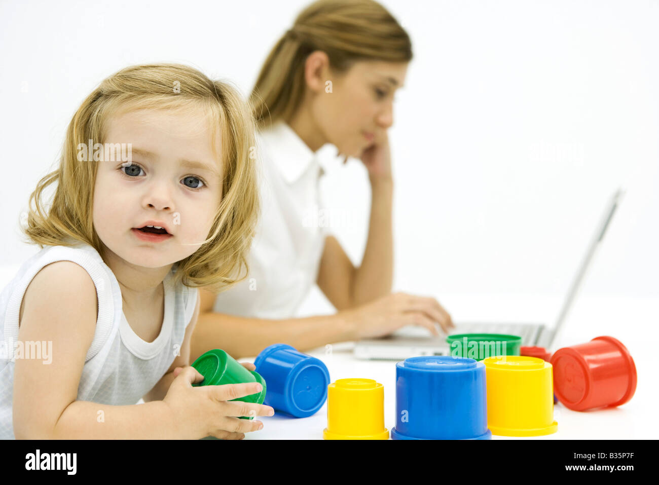 Little girl playing with toys while young woman uses computer in ...