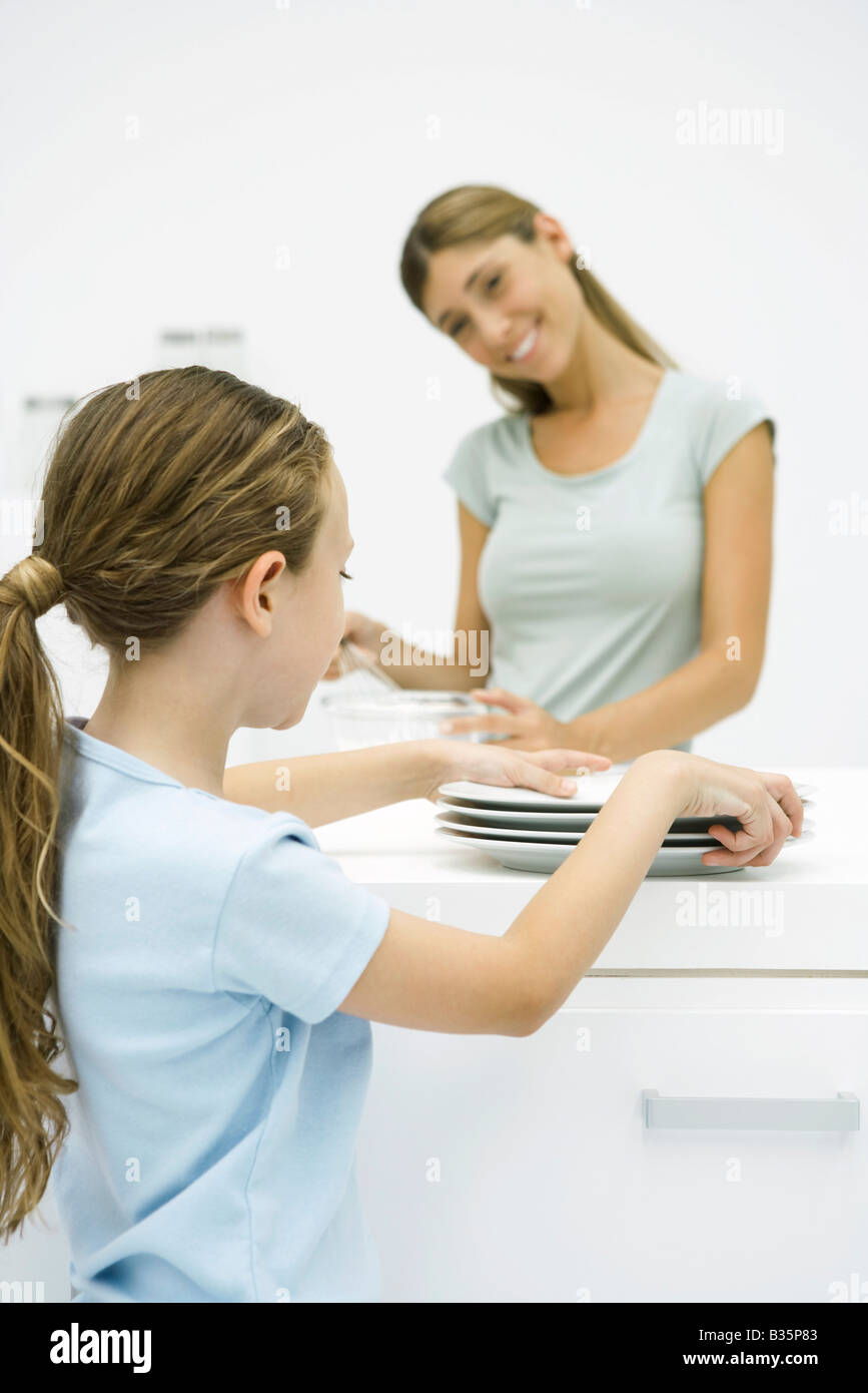 Girl picking up plates, mother smiling at her Stock Photo - Alamy