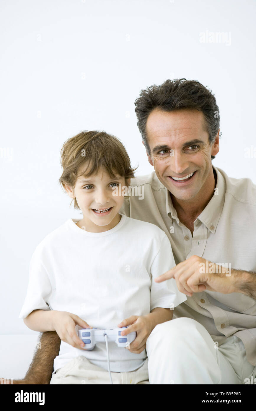 Boy playing video game, father sitting with him, pointing at controller ...