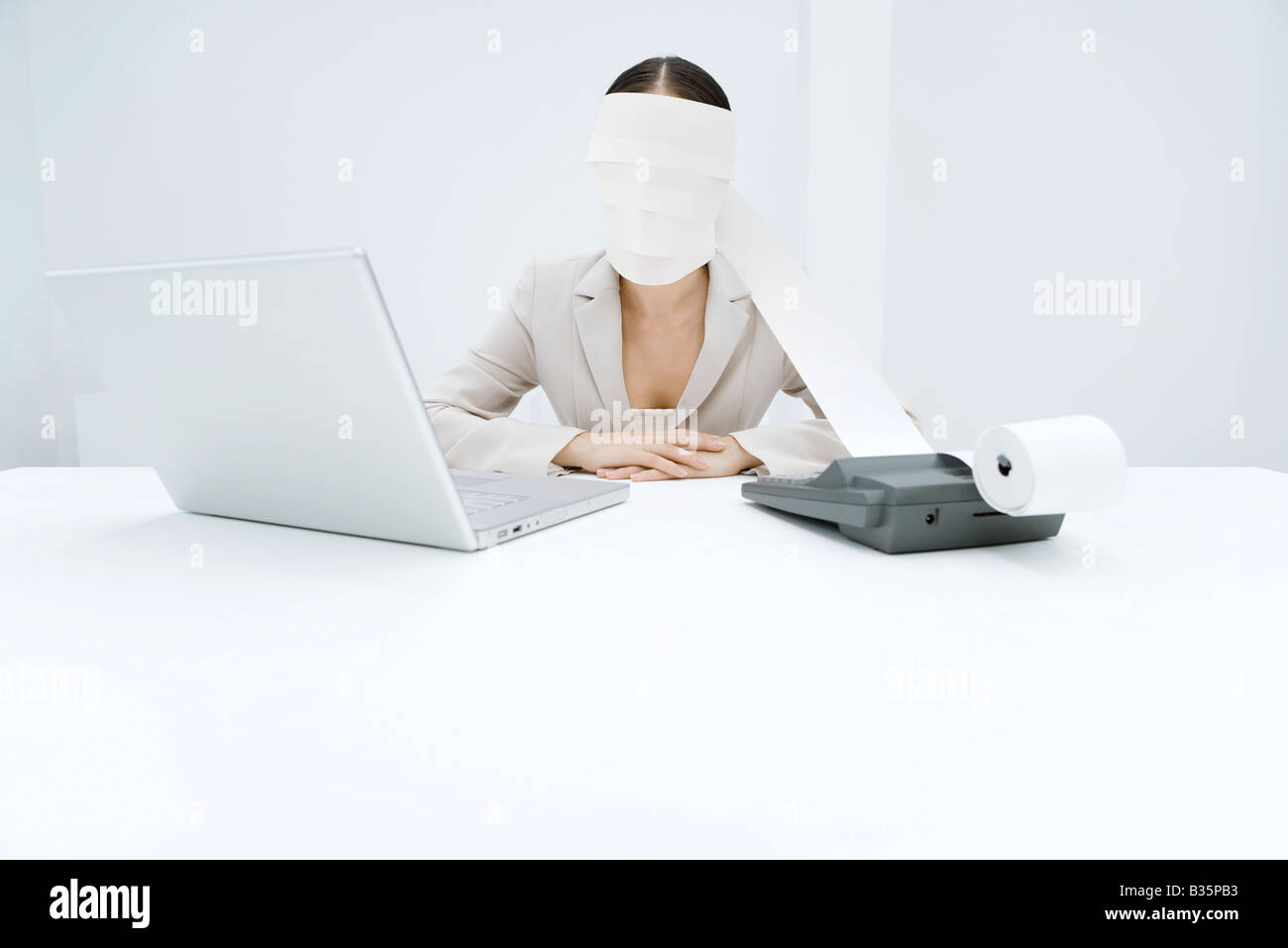 Woman sitting at desk with adding machine and laptop, printout tape ...