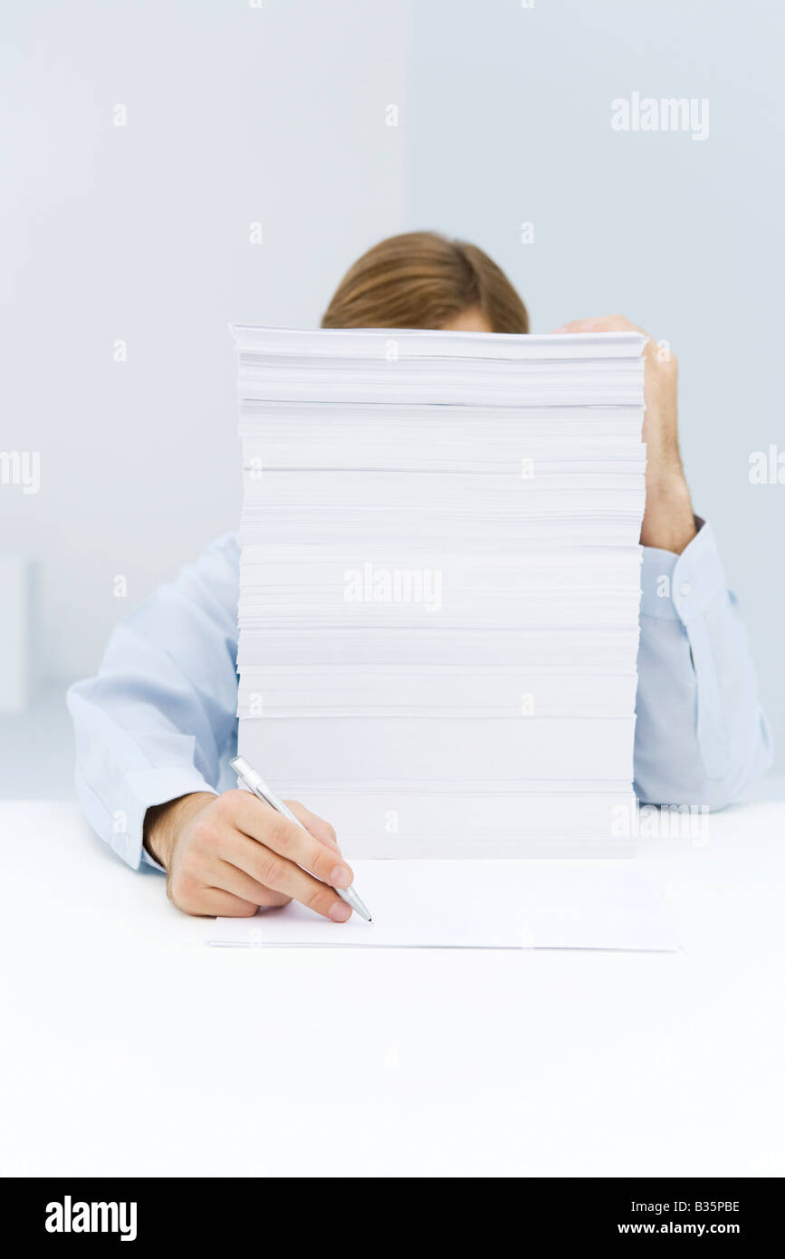 Man hiding behind tall stack of paper, reaching around to write on a ...