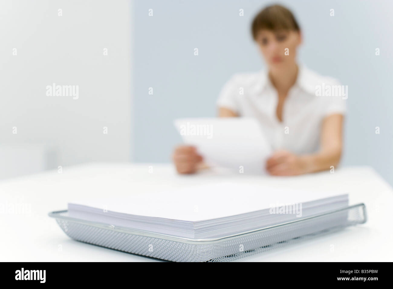 Stack of paper in metal tray, woman reading document in background ...